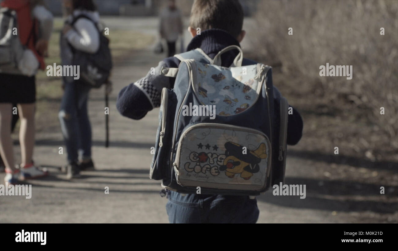 Rear side view of child carrying backpack going to or from school on ...
