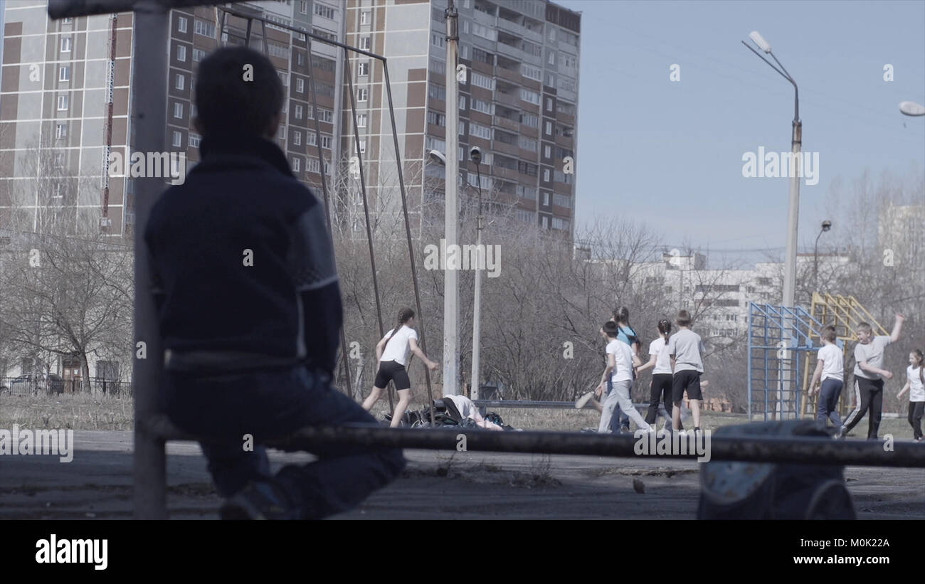 Lonely boy sits on the bench and watches as his friends play football ...
