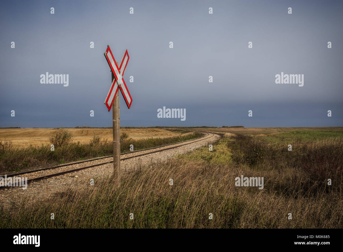A railway crossing sign by a curving railroad through harvested field ...