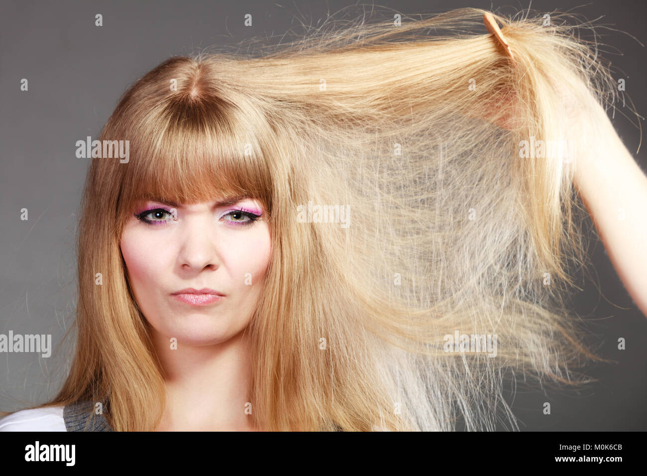 Haircare. Blonde woman with her damaged dry hair angry face expression ...