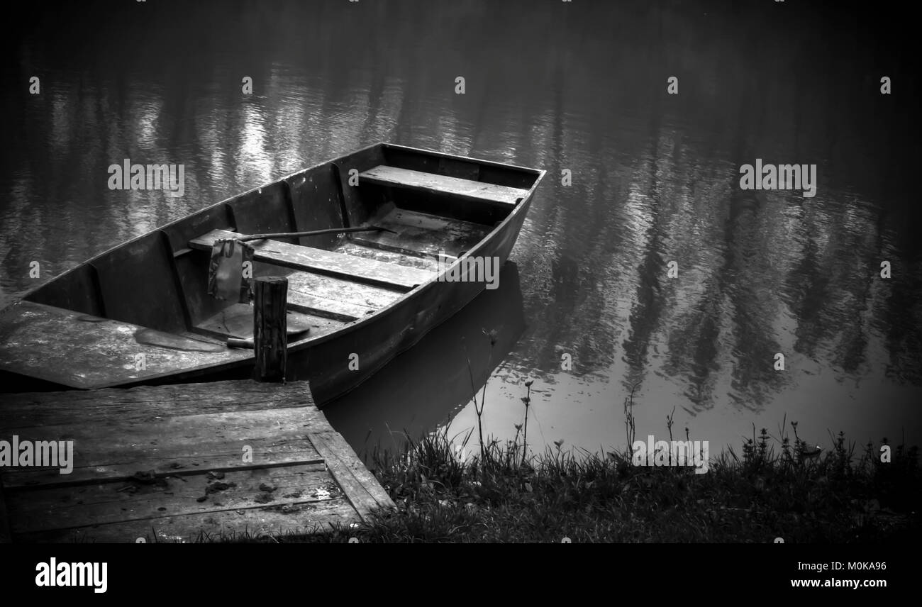 A black and white photo of a small, old boat next to a small dock Stock ...