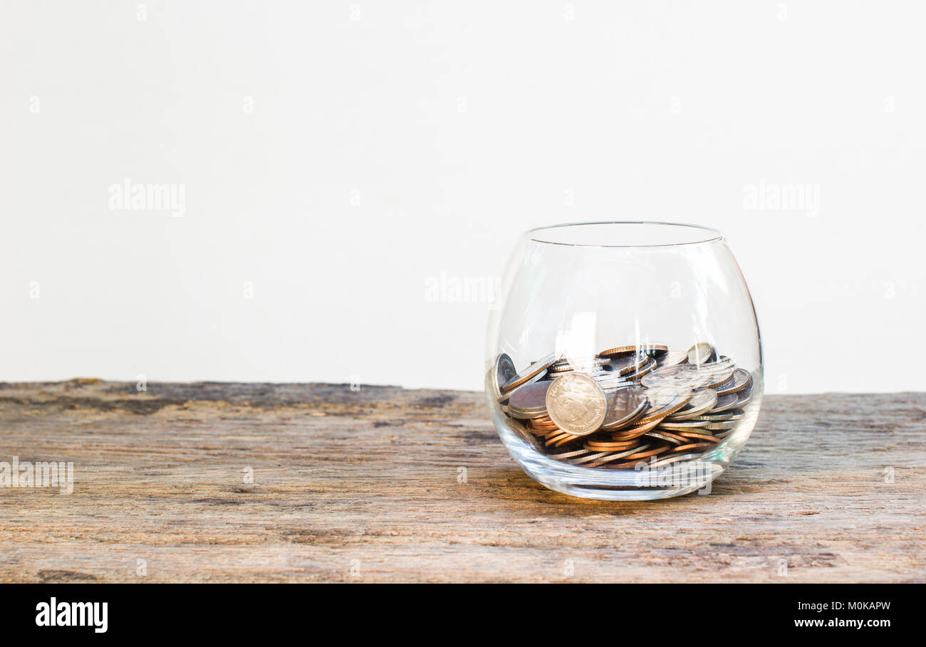 Many coins in clear glass on wooden table on white background with copy ...