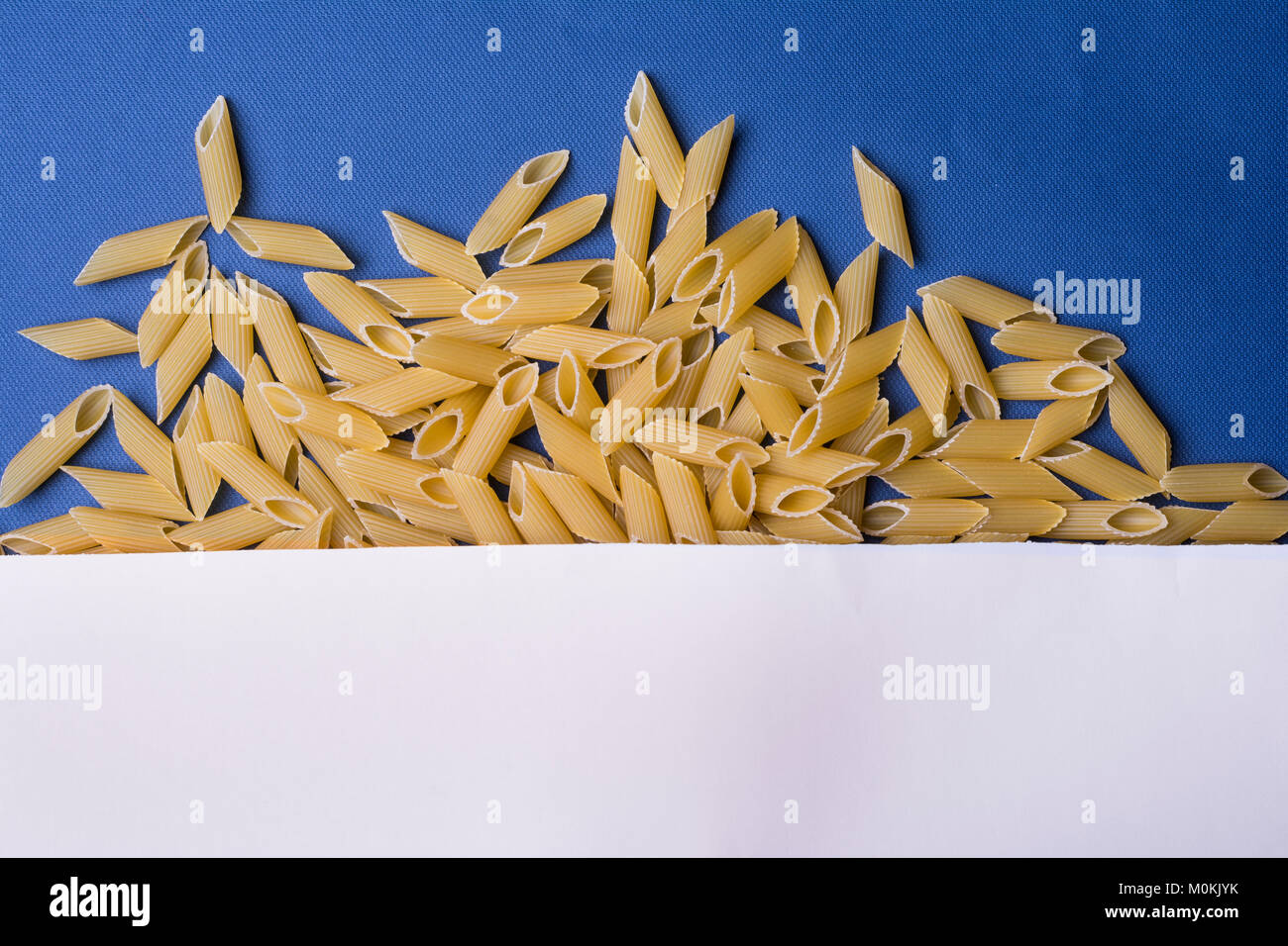 White paper covered tubular penne pasta on blue background. Food ...