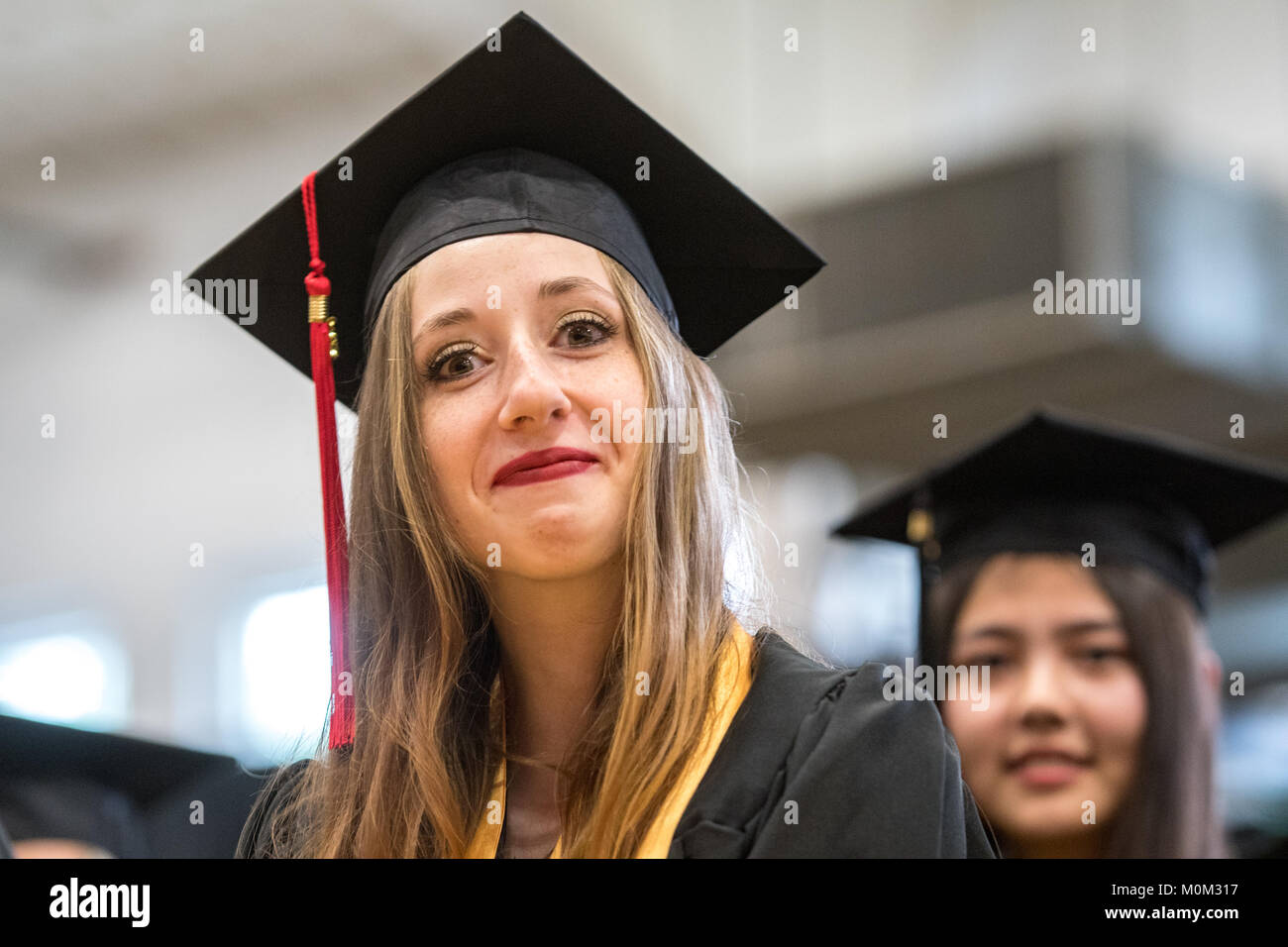 Young woman looks at camera while wearing a graduation cap and gown ...