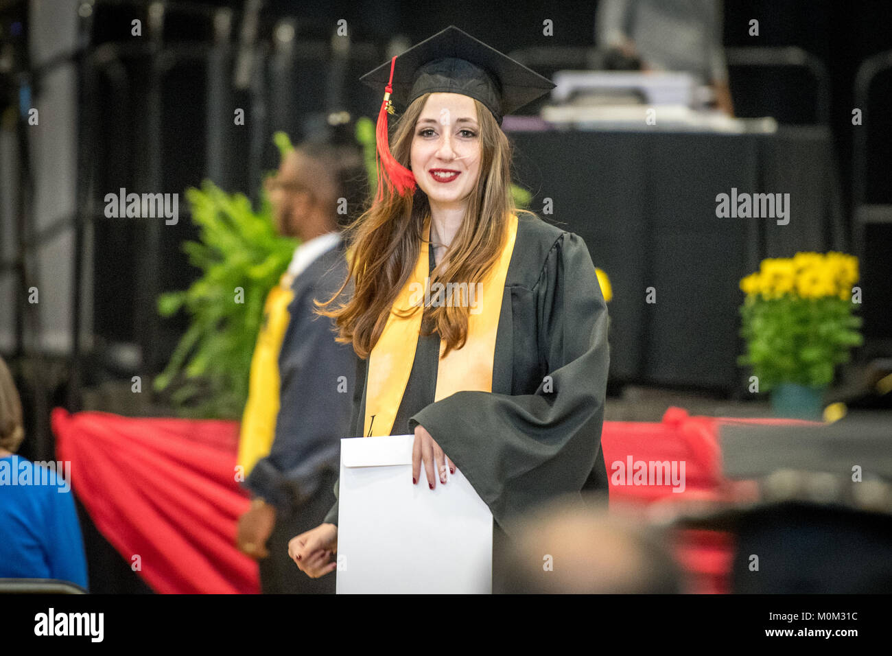 Young woman in graduation cap and gown walks off stage holding her ...