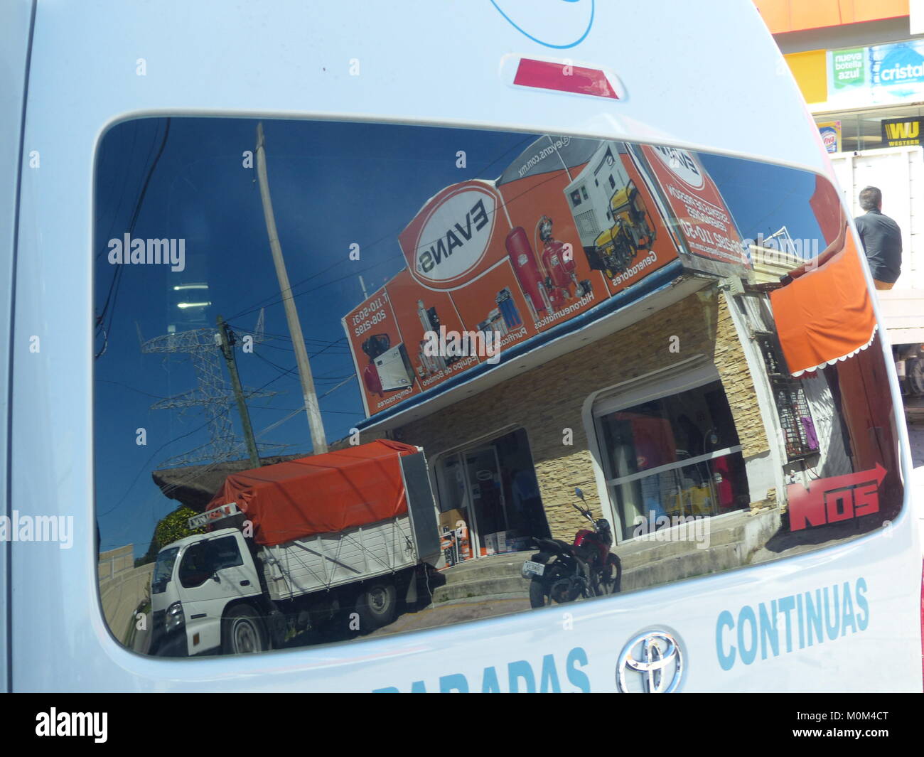 Building and delivery truck reflected in rear glass of passenger van ...