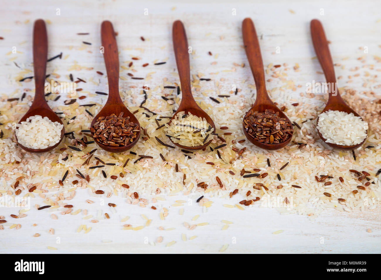 Five spoons with different grades of rice on an old wooden background ...