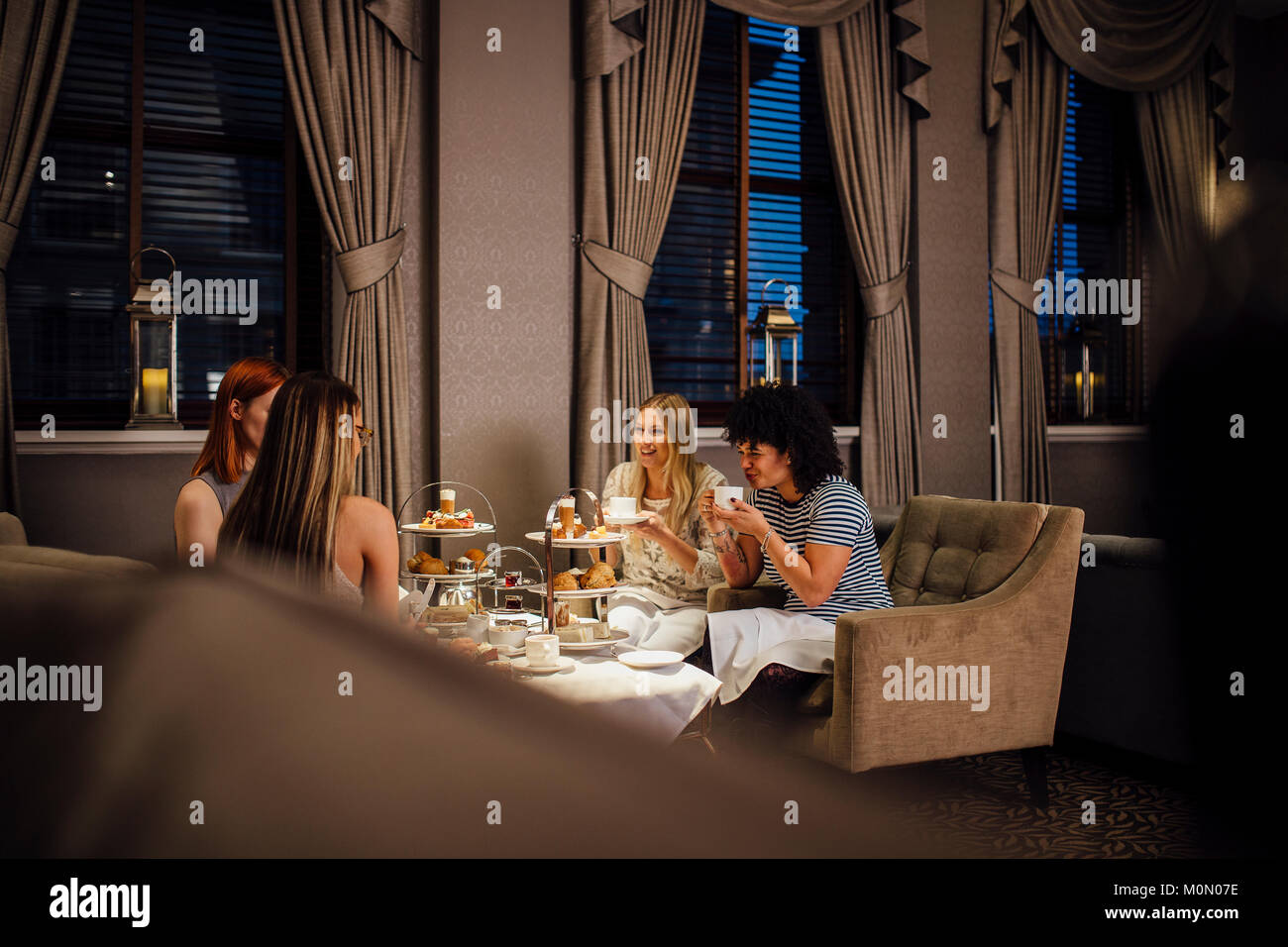 Four women are sitting together enjoying afternoon tea. They are ...