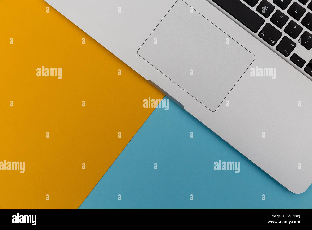 Laptop computer keyboard overhead on bright yellow and blue background ...