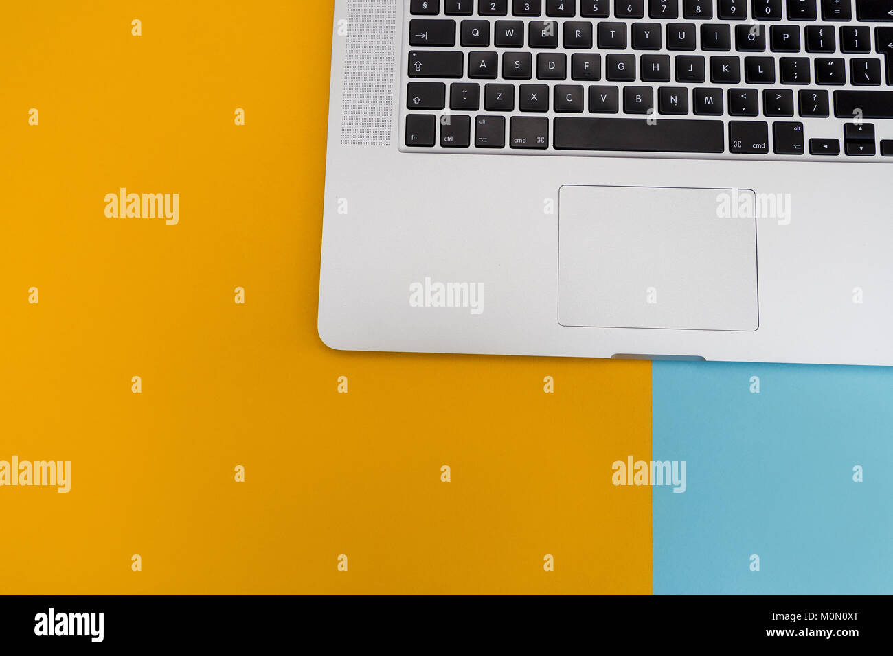 Laptop computer keyboard overhead on bright yellow and blue background ...
