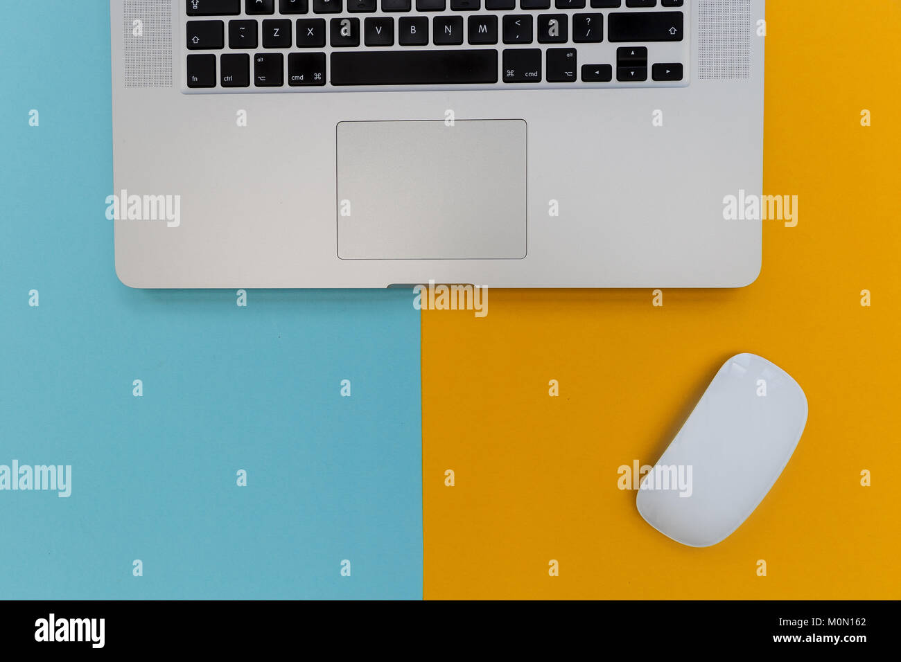 Laptop computer keyboard with mouse overhead on bright yellow and blue ...
