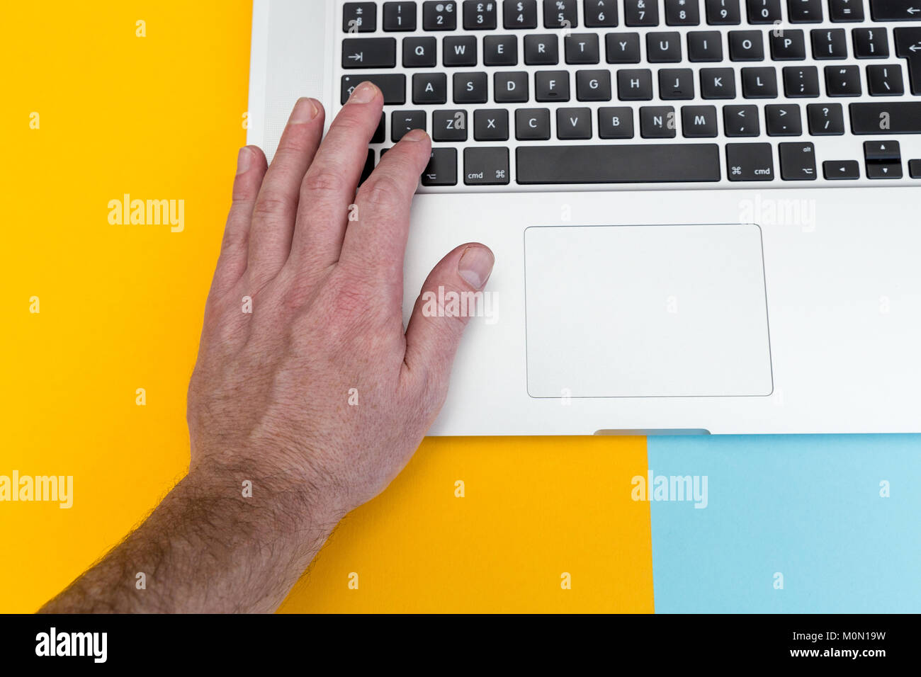 Man's hand typing on laptop computer keyboard overhead on bright yellow ...