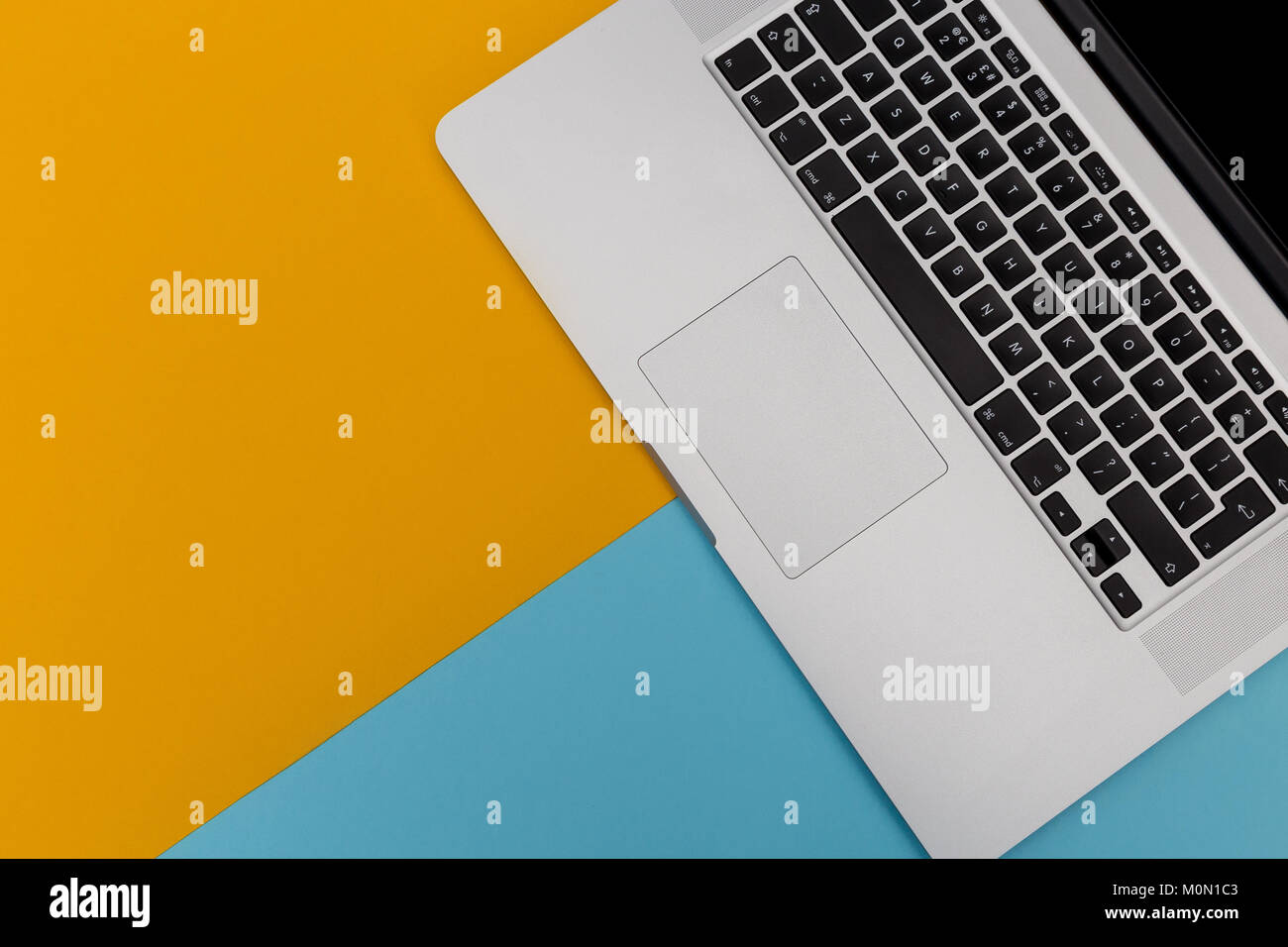 Laptop computer keyboard overhead on bright yellow and blue background ...