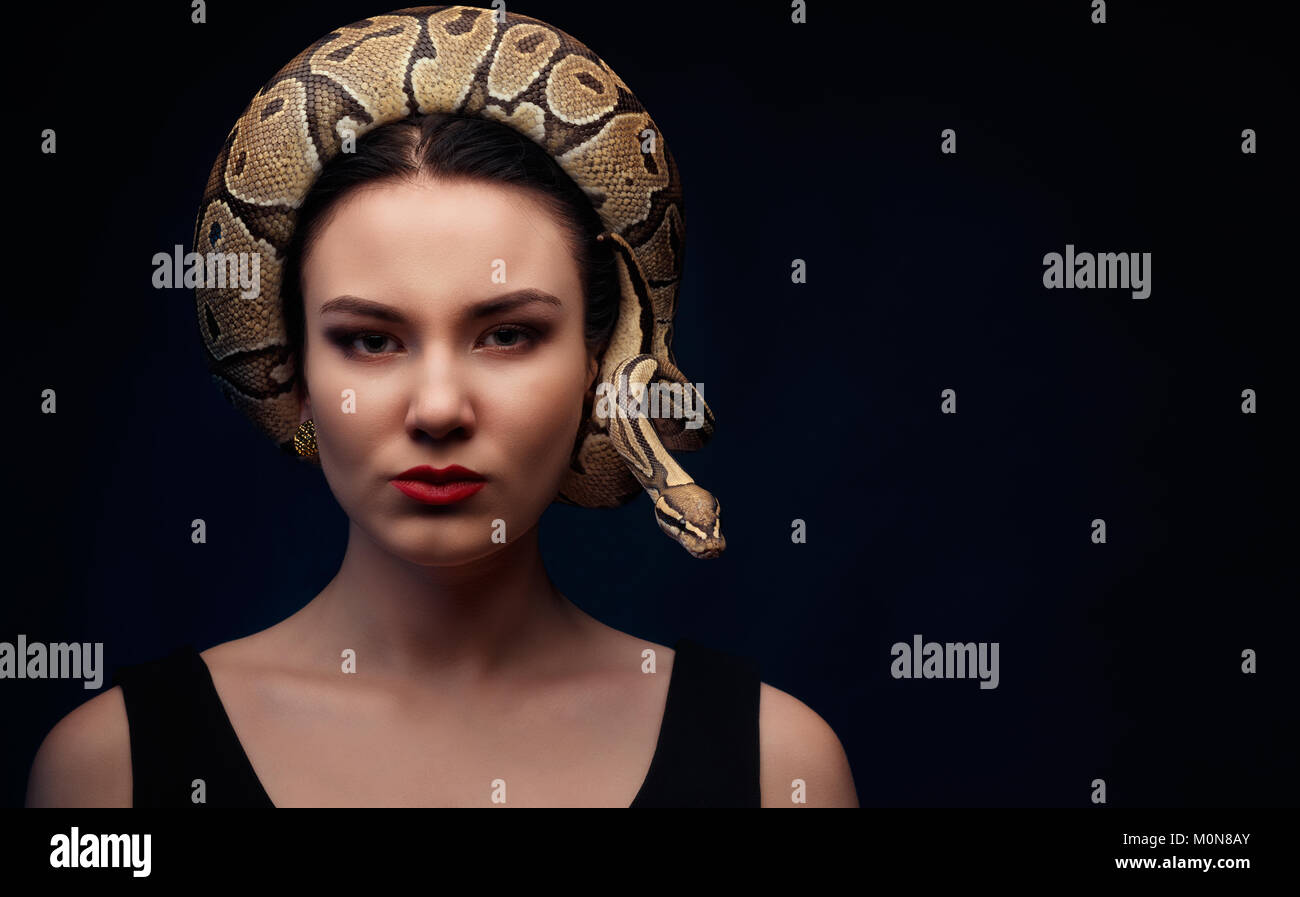 Close up portrait of woman with snake around her head on dark ...