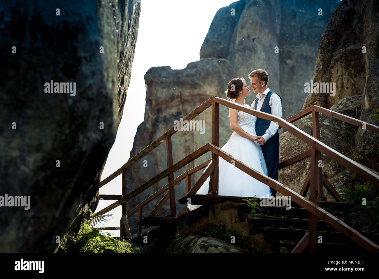 Stylish just married couple is tenderly holding hands while standing on ...