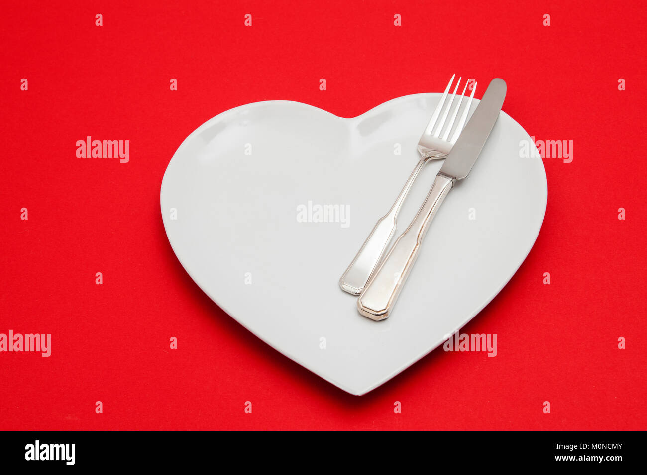 Heart shaped plate with knife and fork on a red background Stock Photo ...