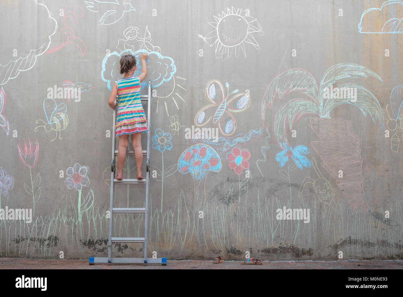 Girl standing on ladder drawing colourful pictures with chalk on a ...