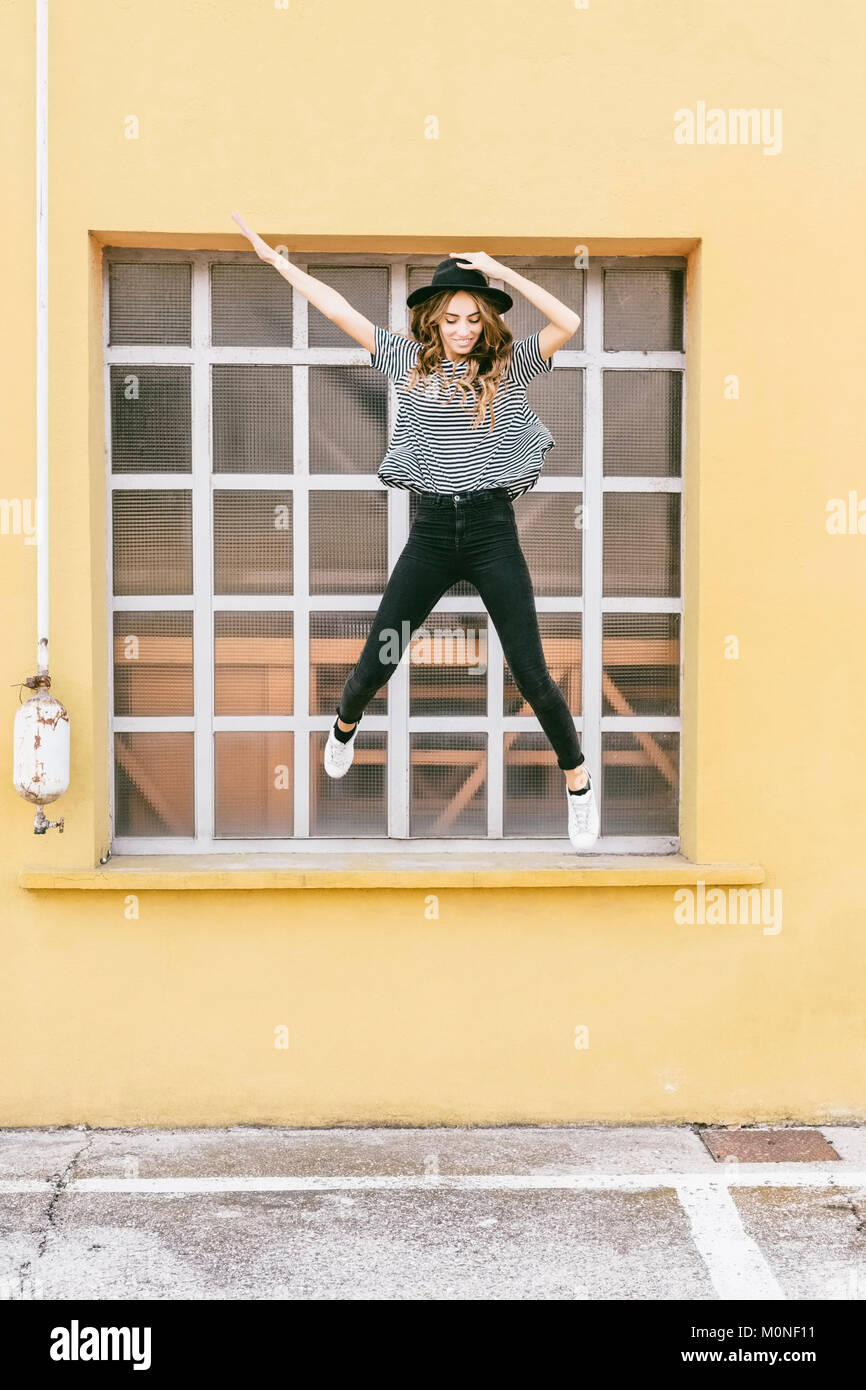 Fashionable young woman wearing hat jumping in the air Stock Photo - Alamy