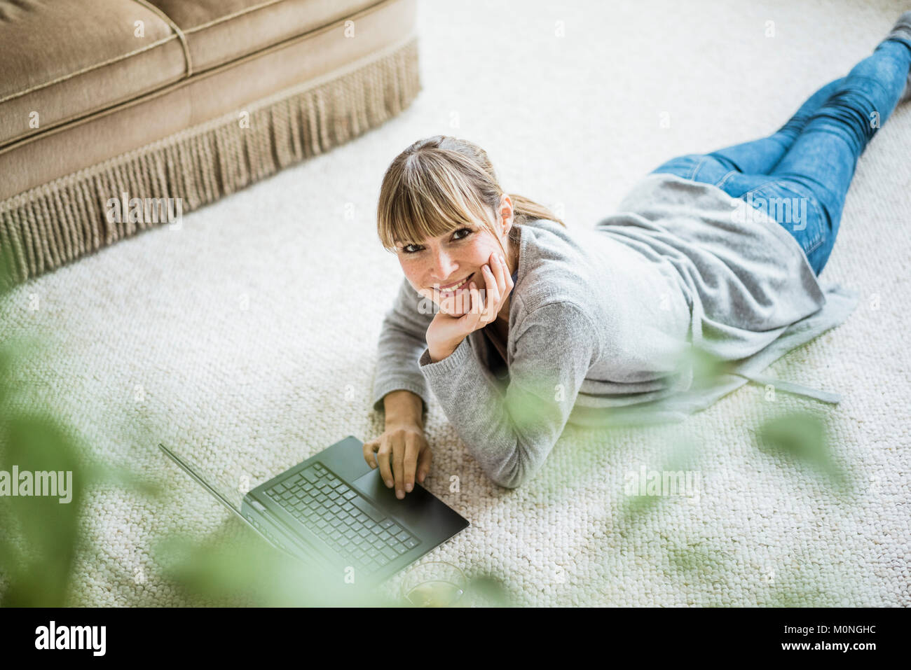 Smiling woman lying on the floor using laptop Stock Photo - Alamy