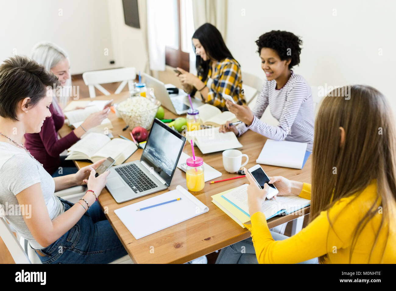 Group of female students using cell phone at table at home Stock Photo ...