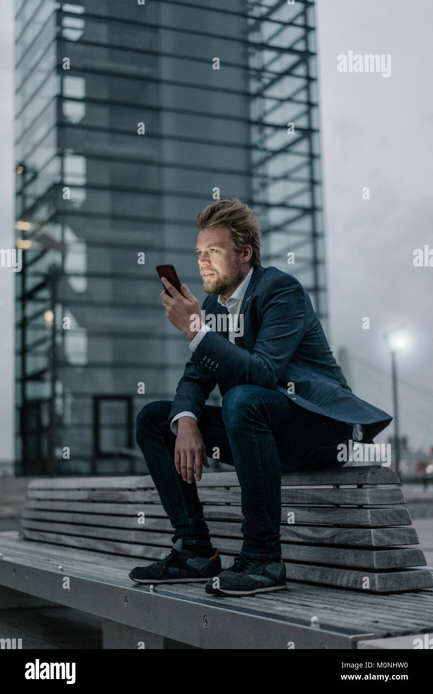 Businessman sitting on bench in the city holding cell phone Stock Photo ...