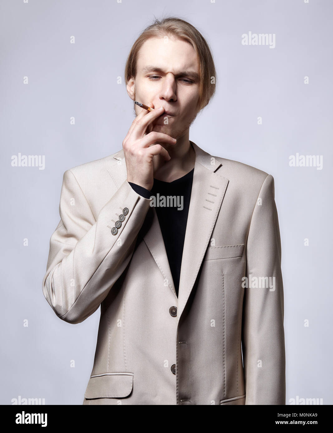 Young blond male model in beige man suit smoking on gray background ...