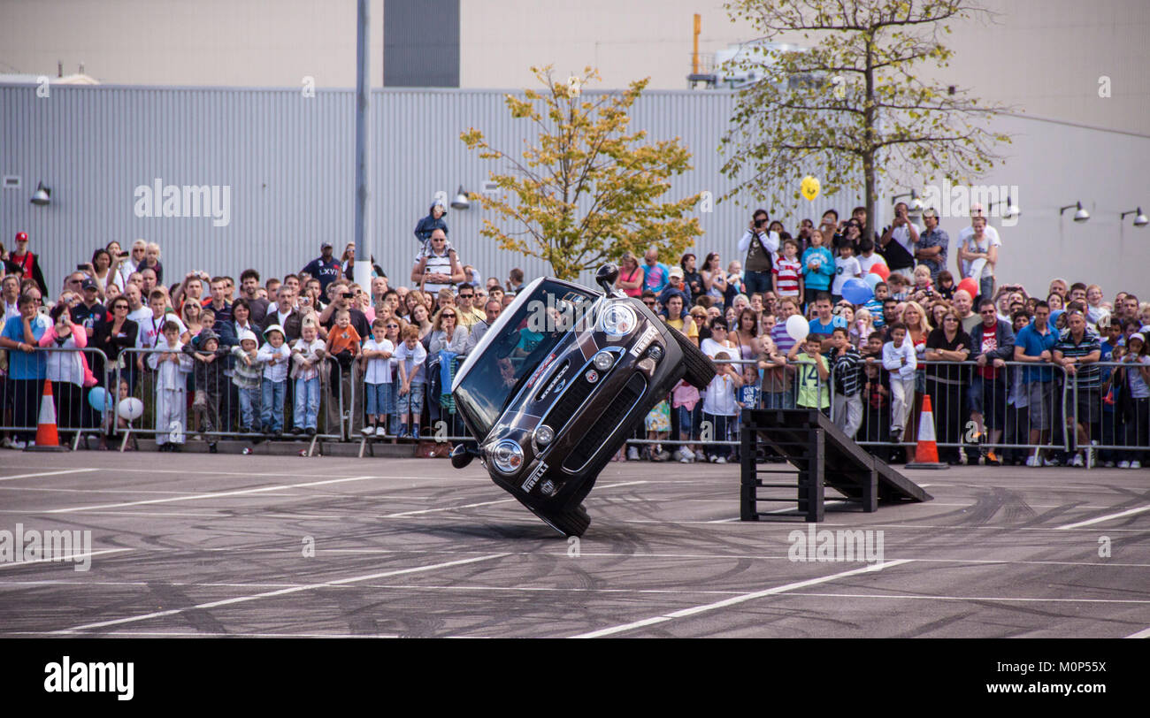 Crowds watch a stunt driver in a new BMW mini drive on two wheels Stock ...