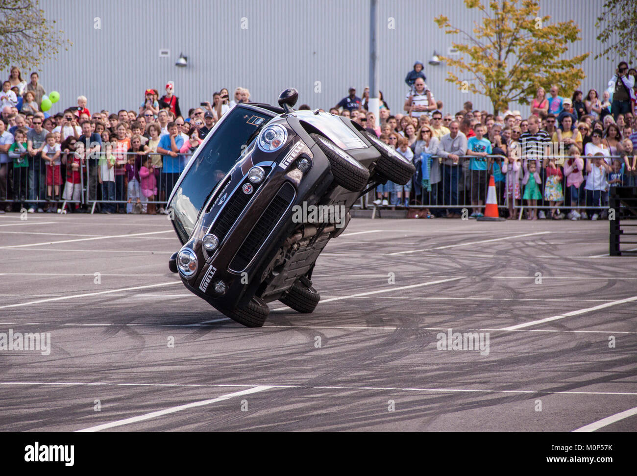 Crowds watch a stunt driver in a new BMW mini drive on two wheels Stock ...