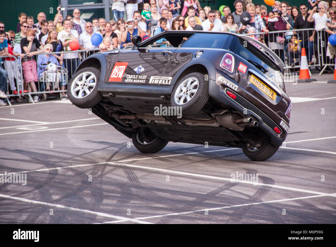 Crowds watch a stunt driver in a new BMW mini drive on two wheels Stock ...