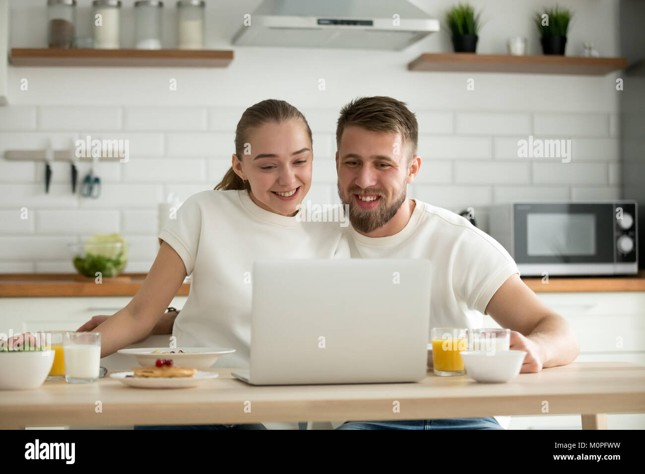 Smiling couple watching funny video on computer while having bre Stock ...