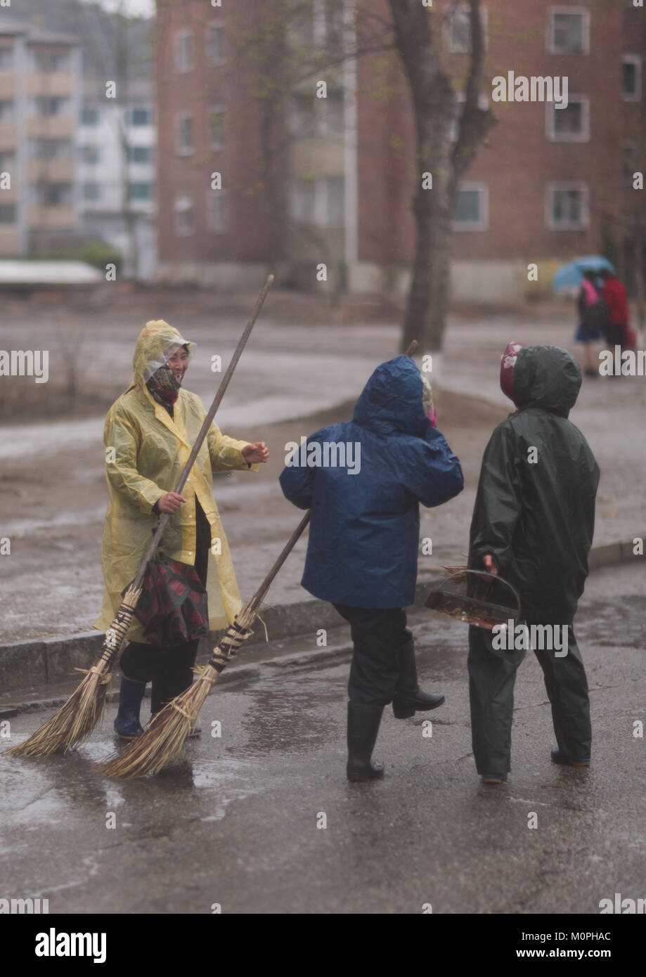 North Korean people cleaning the road with brooms under the rain ...