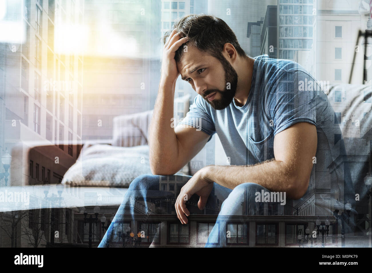 Sad exhausted man sitting and holding hand near head Stock Photo - Alamy