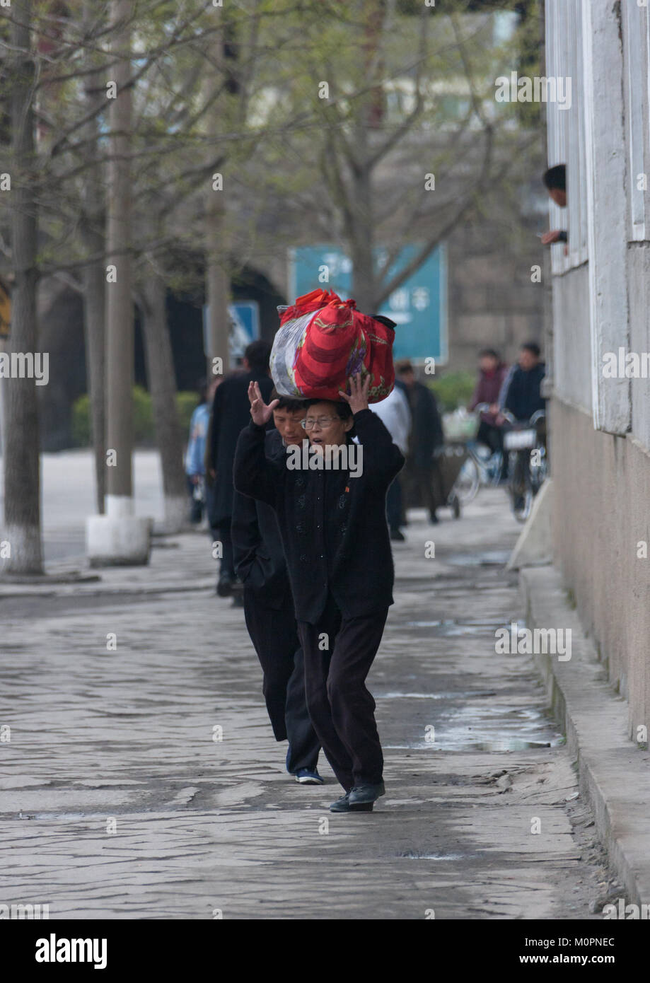 North Korean woman carrying heavy stuff on her head in the street ...