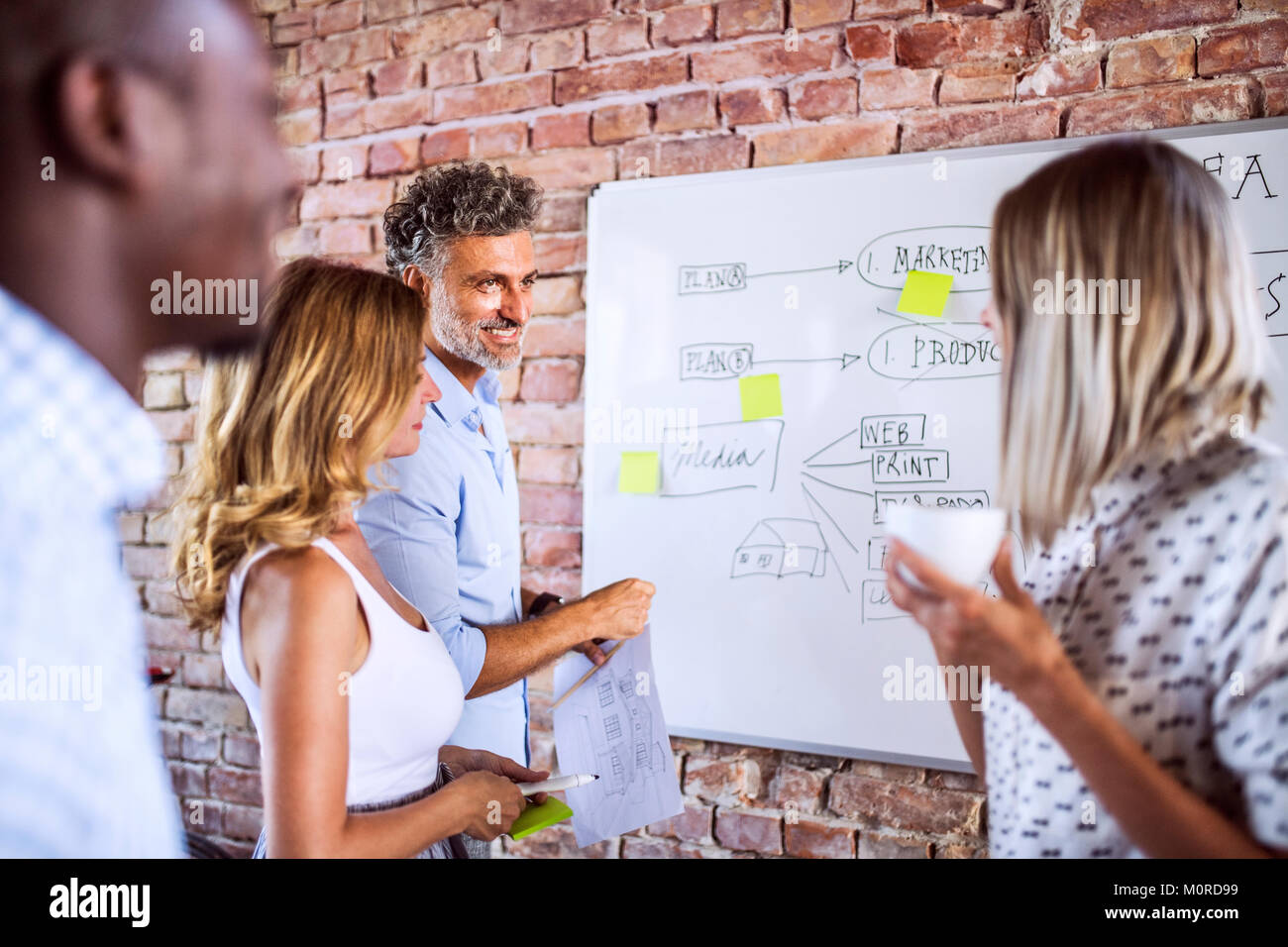 Business team working together on whiteboard at brick wall in office ...