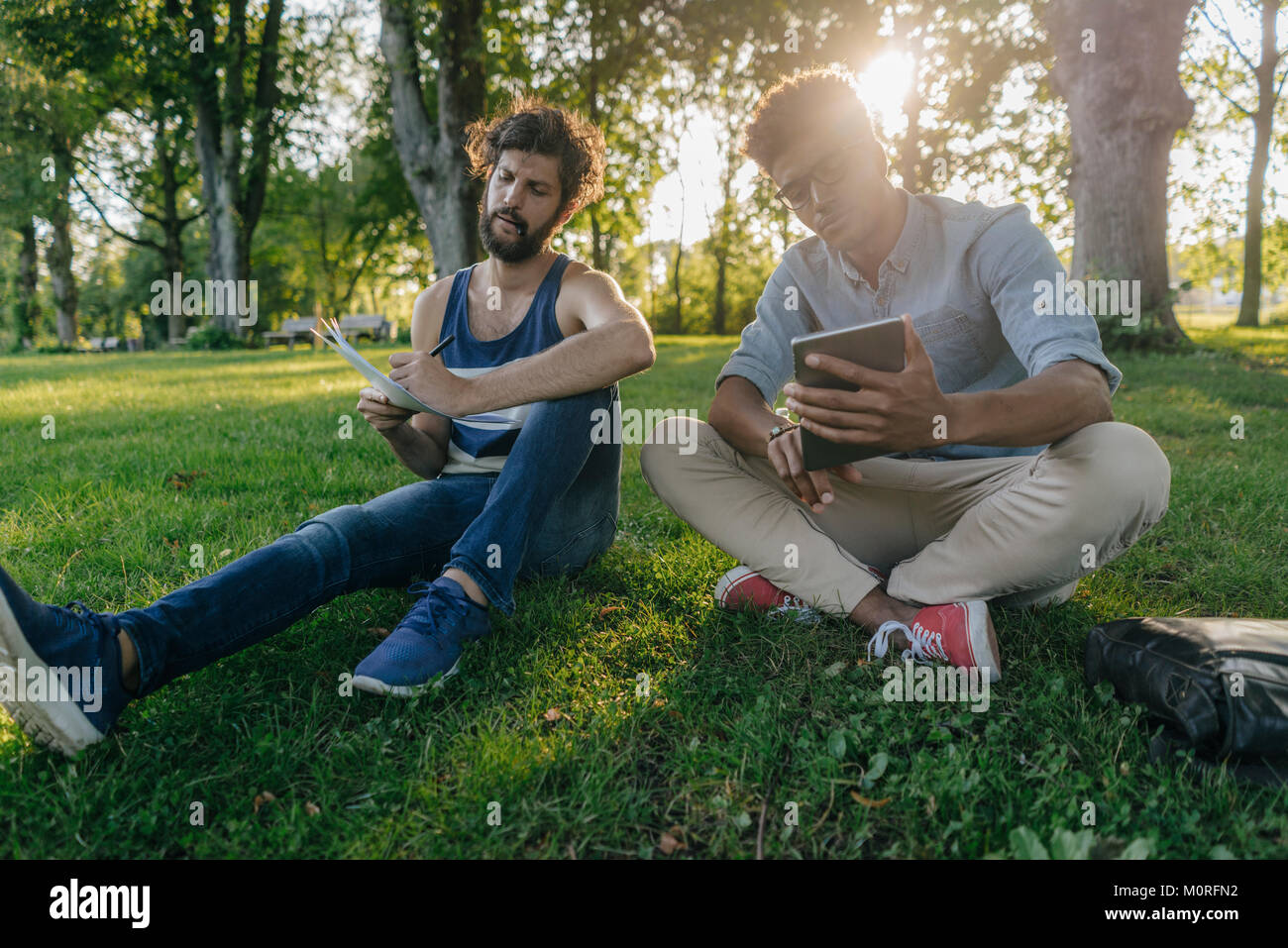 Two friends sitting in a park with mobile device and papers Stock Photo ...