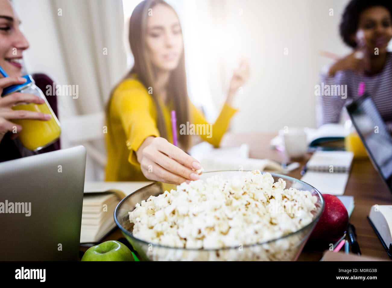 Female student with friends taking popcorn from bowl at table at home ...