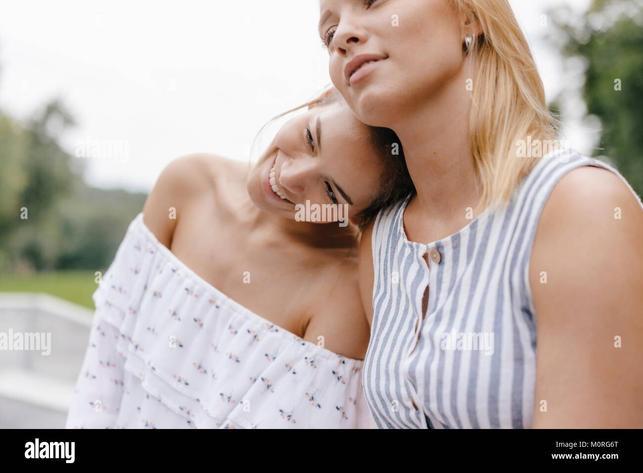 Smiling young woman resting on female friend's shoulder Stock Photo - Alamy