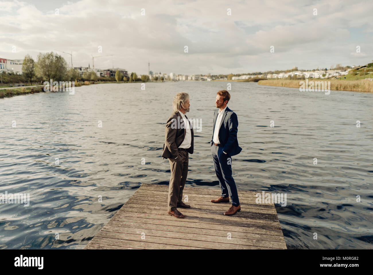 Two businessmen standing on jetty at a lake talking Stock Photo - Alamy