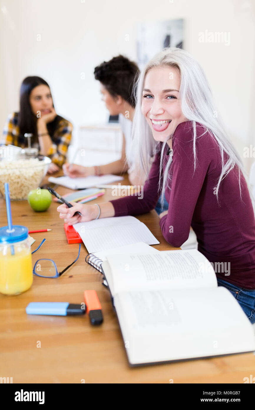 Portrait of happy female student at table at home with friends in ...