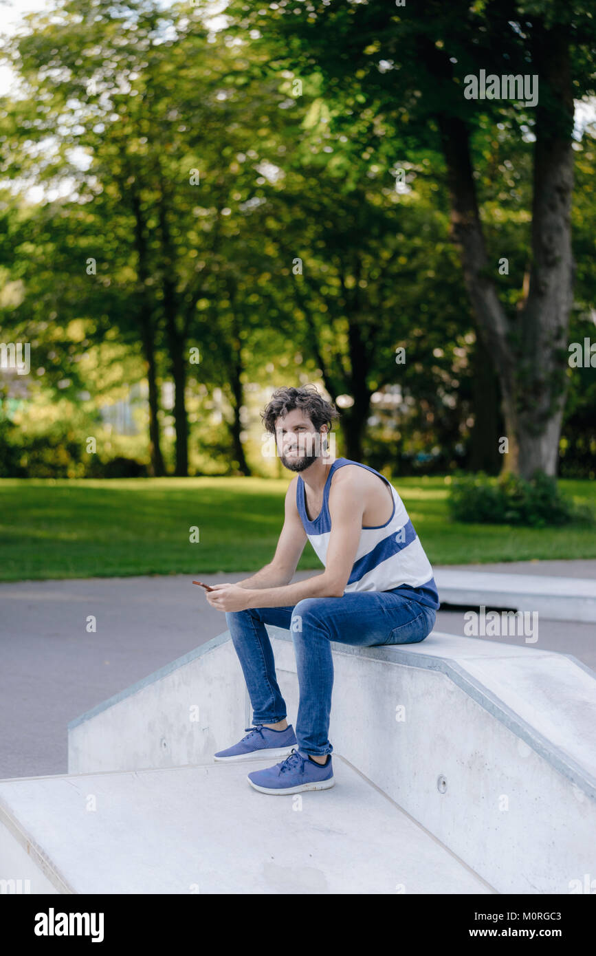 Man with cell phone sitting in skatepark Stock Photo - Alamy