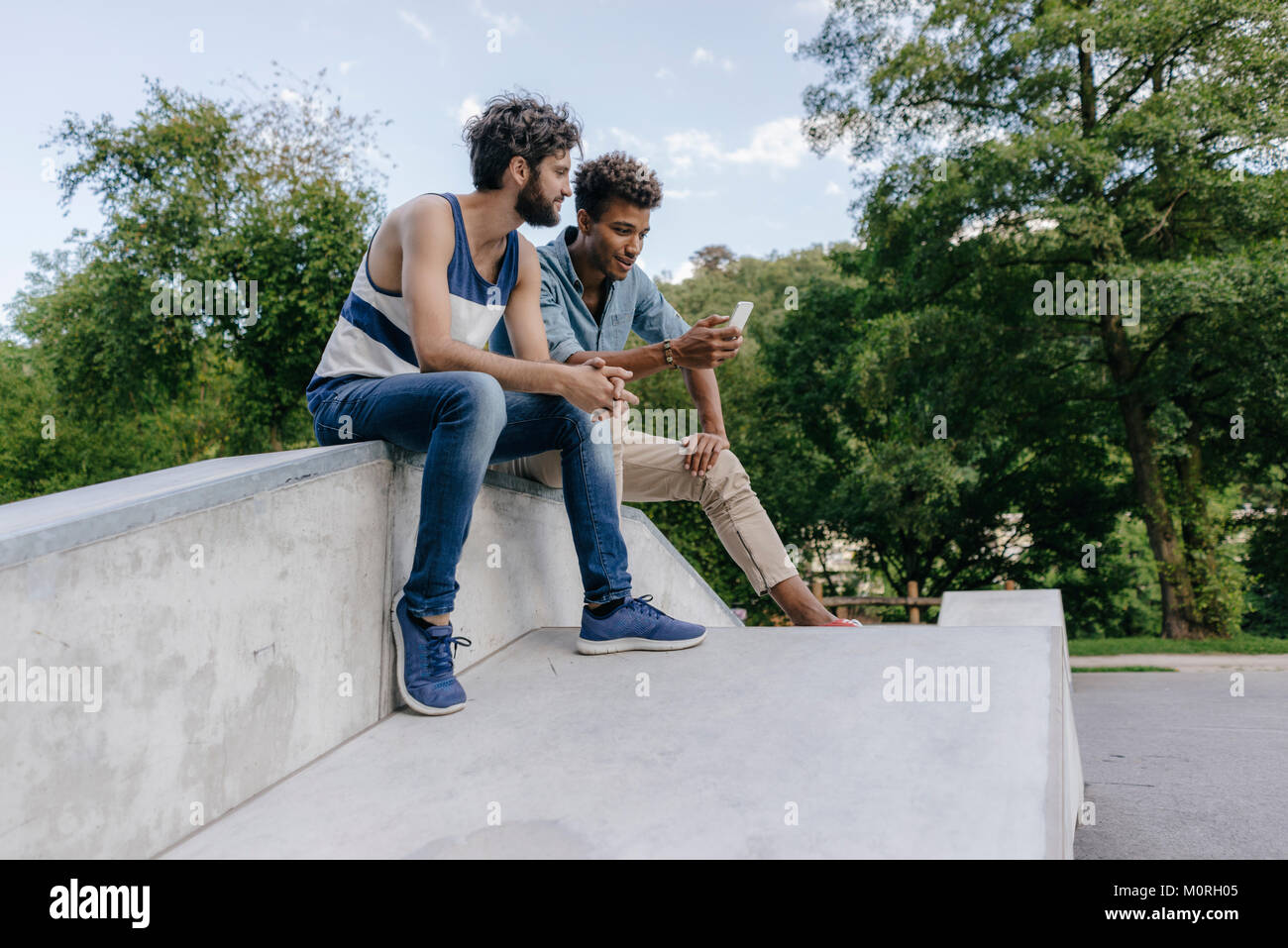 Two friends sharing cell phone in skatepark Stock Photo - Alamy