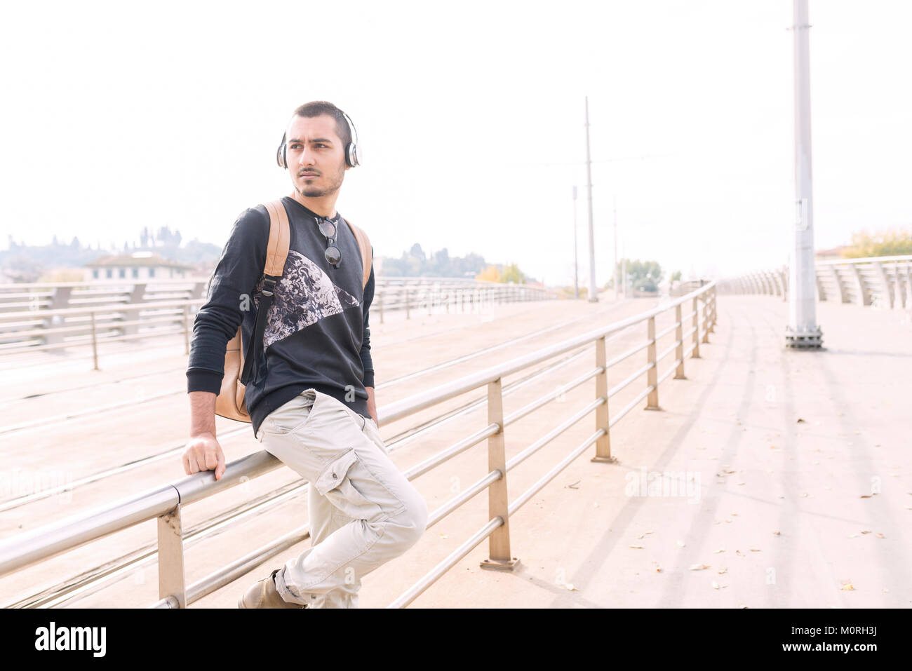 Young man with headphones and backpack at railing outdoors Stock Photo ...
