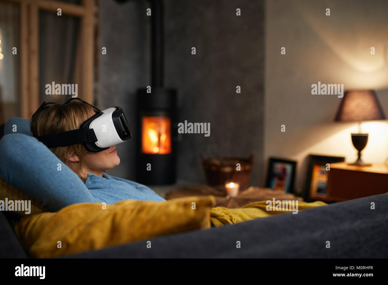 Woman lying on couch at home in the evening using Virtual Reality ...
