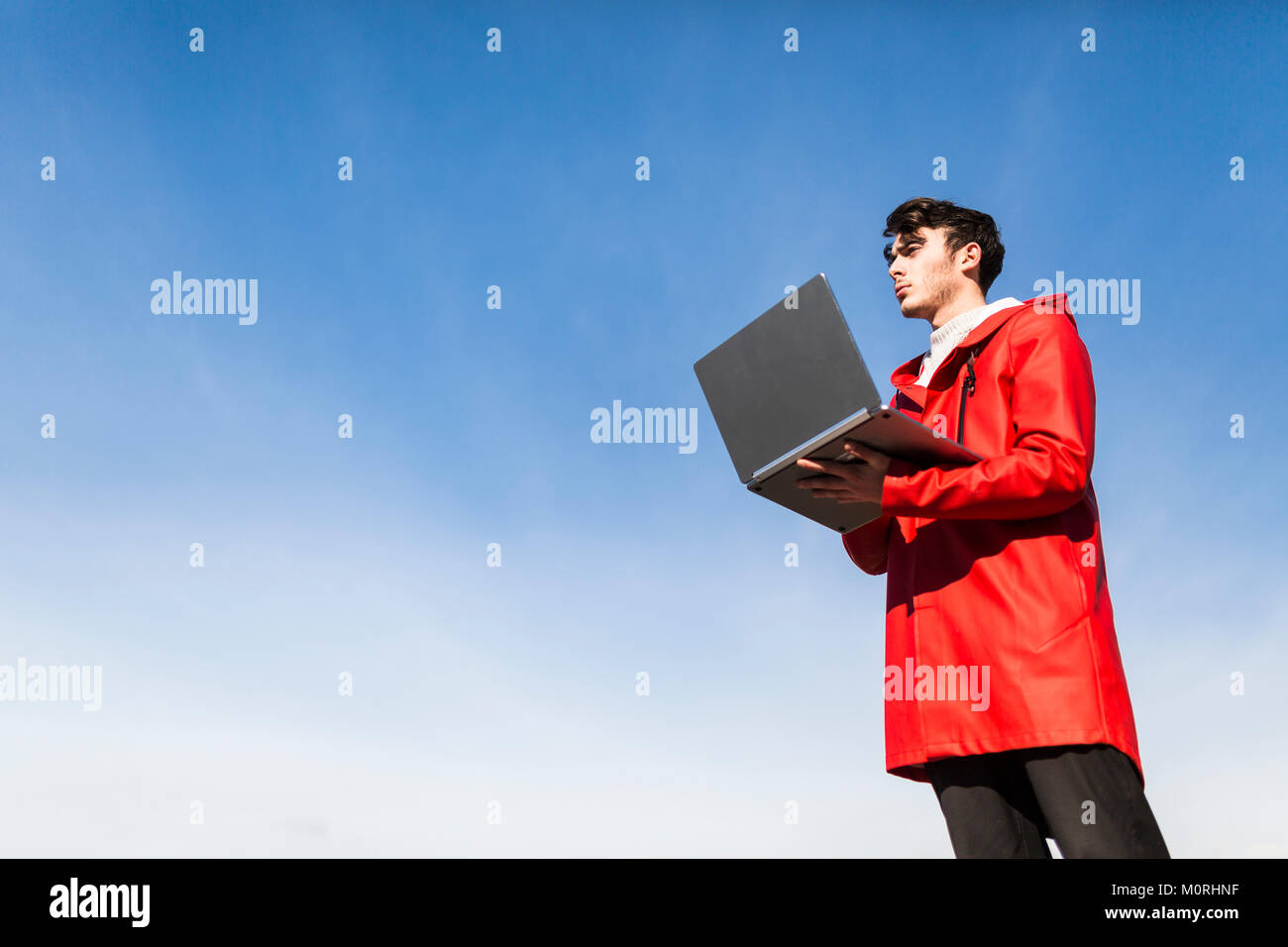 Blue sky, young man using laptop Stock Photo - Alamy