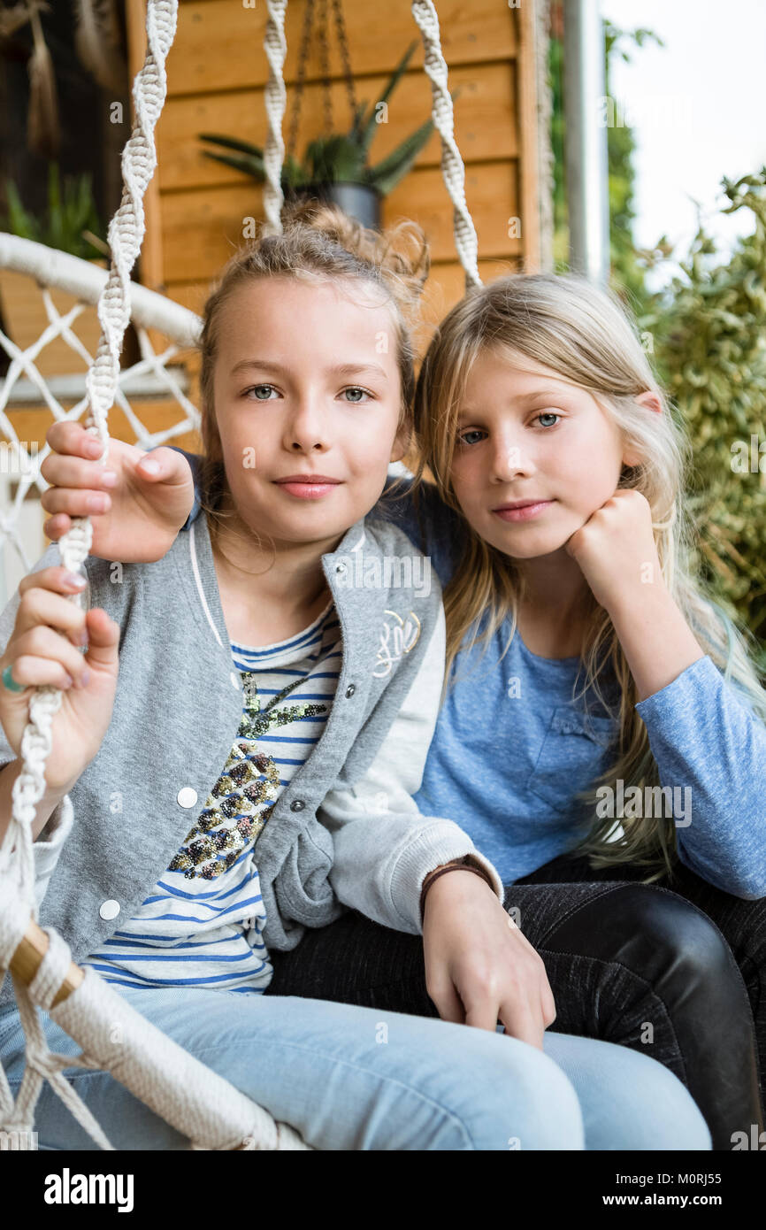 Portrait of two best friends sitting in a hanging chair on veranda ...