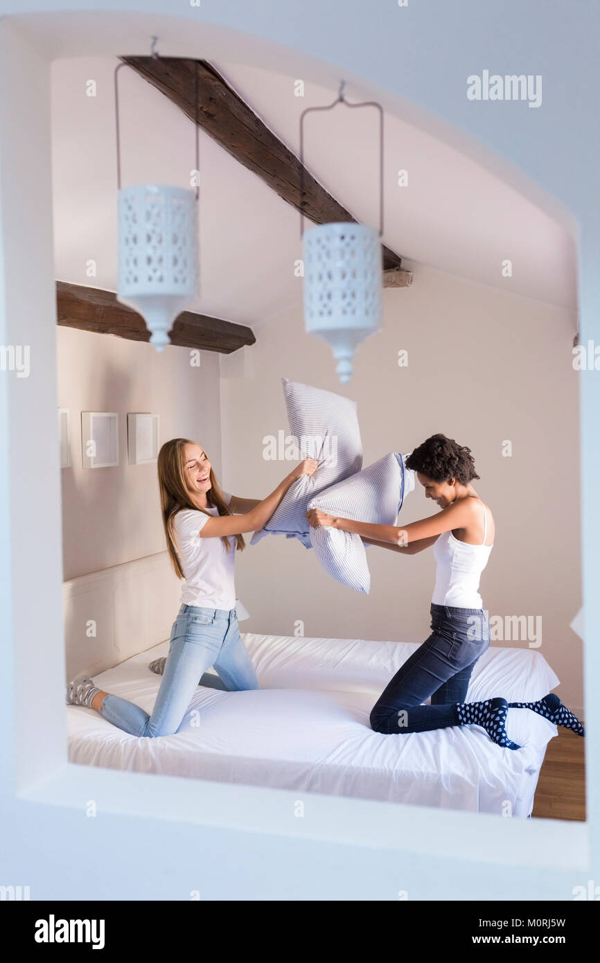 Playful female friends having a pillow fight in bed Stock Photo - Alamy