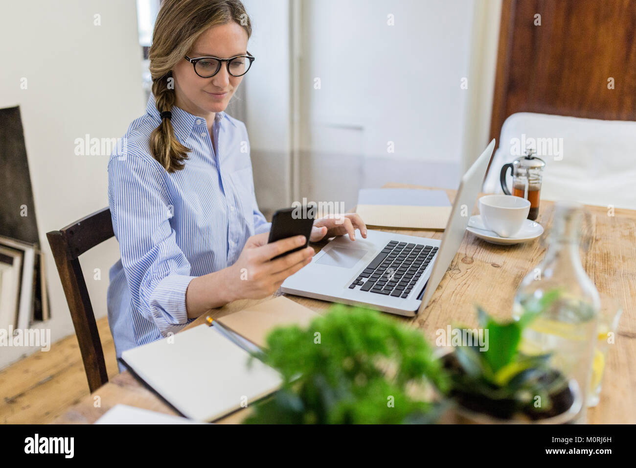 Woman using cell phone and laptop on wooden desk at home Stock Photo ...