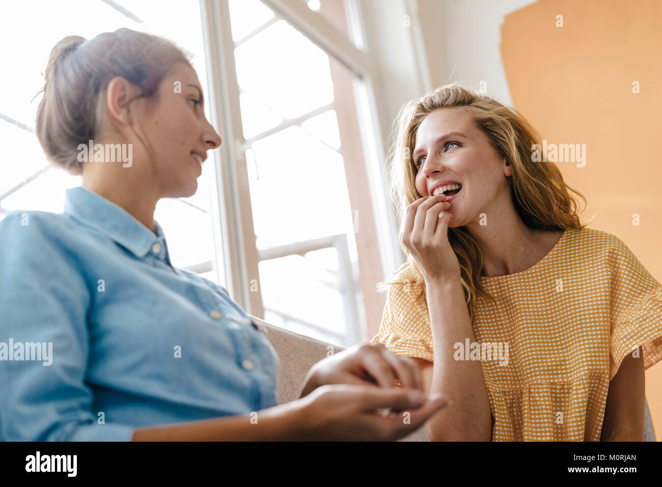 Two young women sitting on couch talking Stock Photo - Alamy