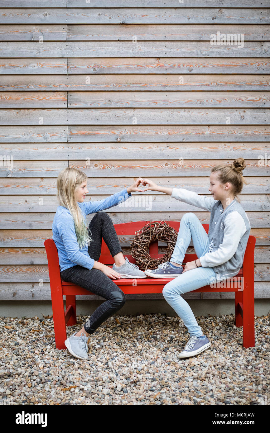 Two best friends sitting on a red bench in front of a wooden facade ...