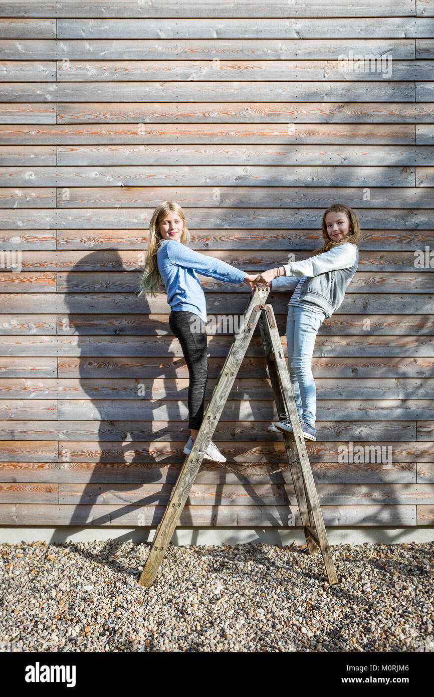 Two girls standing on a ladder in front of a wooden facade Stock Photo ...